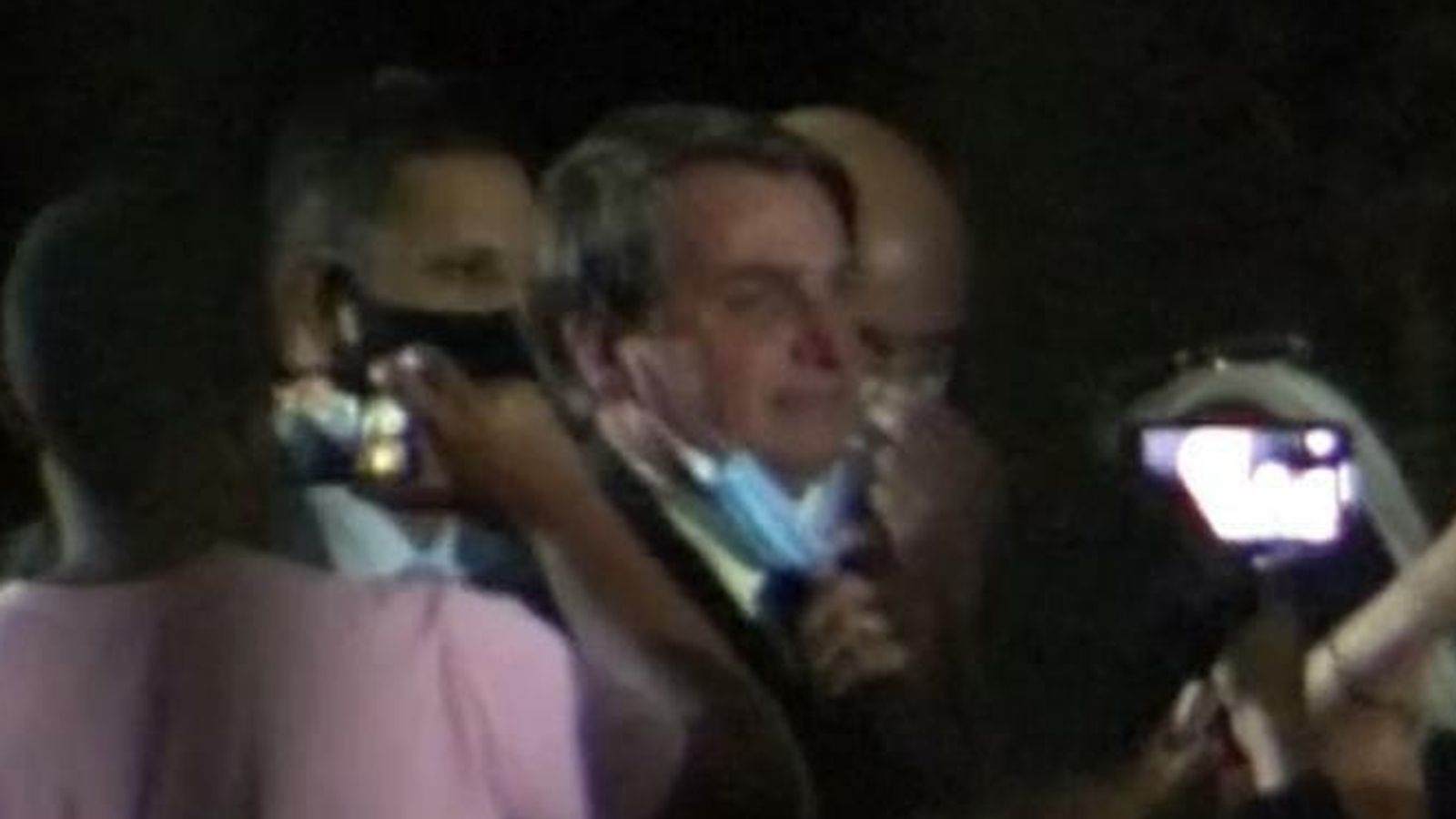 Brazil's president Bolsonaro tucks mask under his chin to greet ...