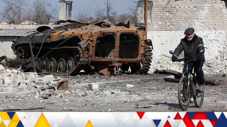 A local resident rides a bicycle past a charred armoured vehicle during ...
